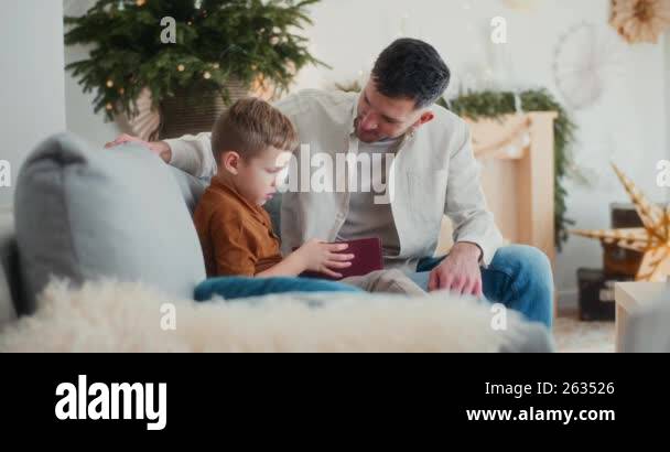 A father encourages his son to read a book with care and patience ...