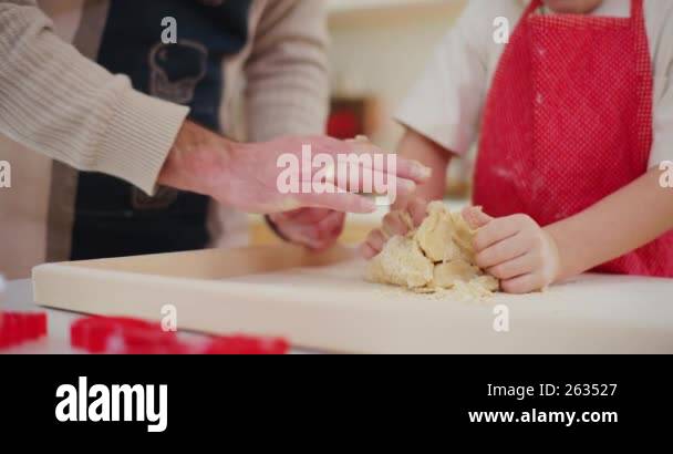 A father helps his son knead bread dough by hand in the kitchen ...