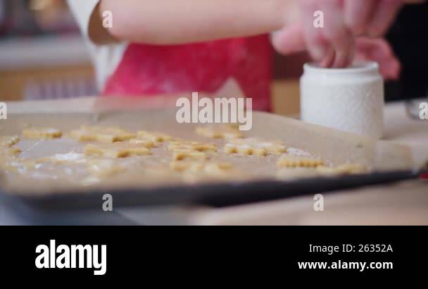 A close-up view of a young boys hand sprinkling sugar on cookies ...