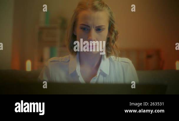 A close-up of a woman focused on her laptop screen, working late in the ...