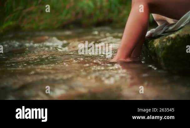 A close-up of a womans legs splashing and playing in the cool, refreshing river water, enjoying ...