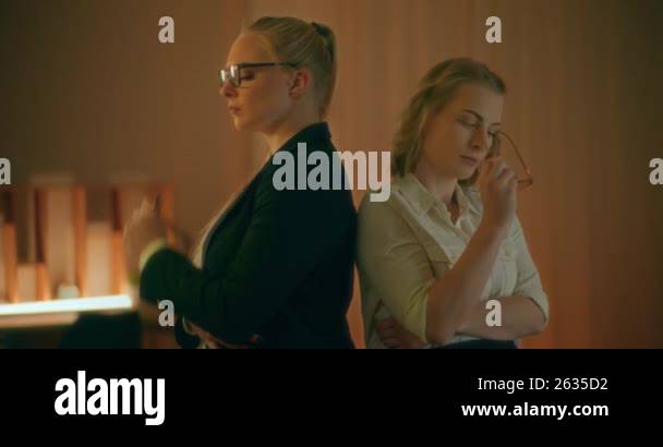 Two women stand back to back in this close-up shot, their posture ...