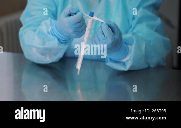 A doctor in a blue protective suit opens the sterile packaging of a ...