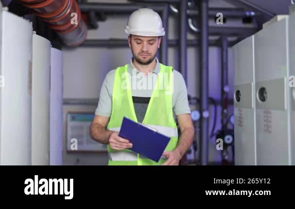 Serious male engineer in boiler room, wearing safety helmet and vest ...