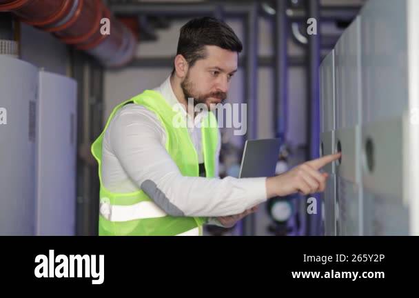 Bearded man in uniform with laptop in boiler room. Engineer or plumber ...