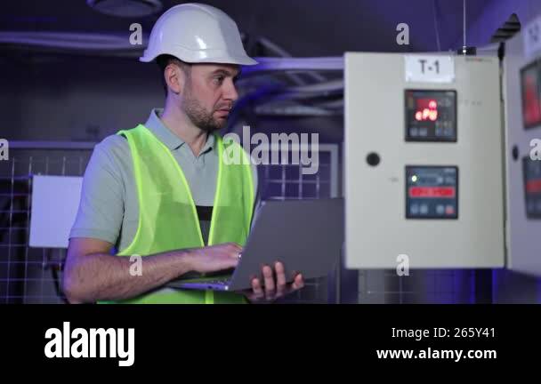 Serious electrical engineer works with laptop next to electrical ...
