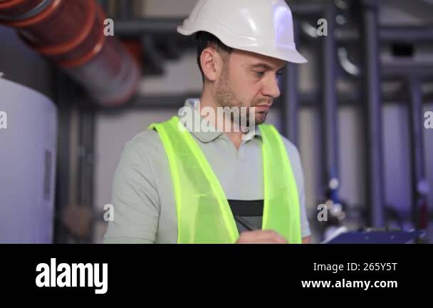 Serious male engineer in boiler room wearing safety helmet and vest ...