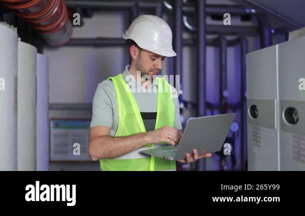 Confident male engineer in a boiler room types on a laptop and closes ...