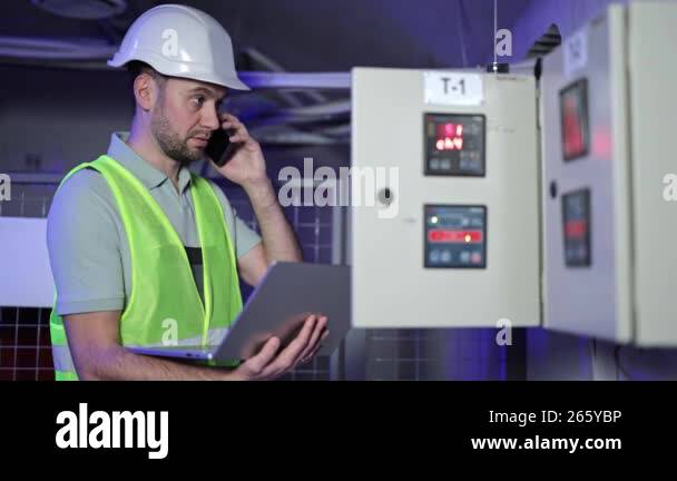 Serious electrical engineer talking on phone and holding laptop ...