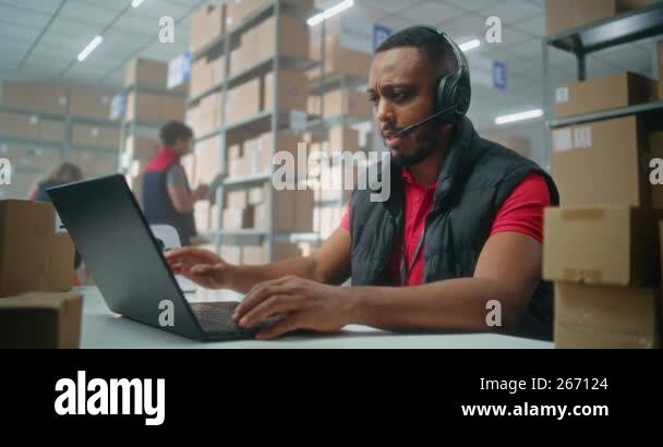 Portrait of African American logistics coordinator in headset talking to client, working on ...