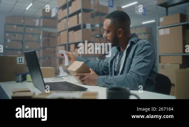 African American warehouse clerk scans parcel with barcode scanner, uses laptop, works in post ...