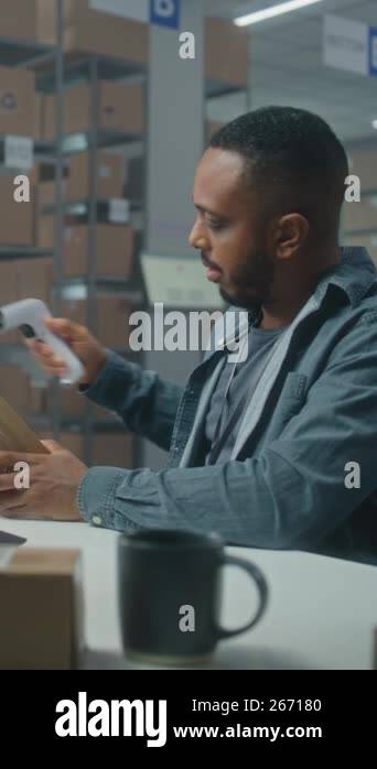 African American logistics manager scans parcel with barcode scanner, talks to colleague, uses ...