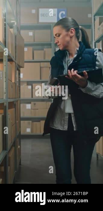 Female Warehouse Associate Scans Cardboard Boxes with E-Commerce Goods on Shelves with Scanner ...