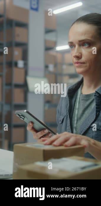 Female inventory clerk scans parcel using smartphone, enters data on computer, works with E ...