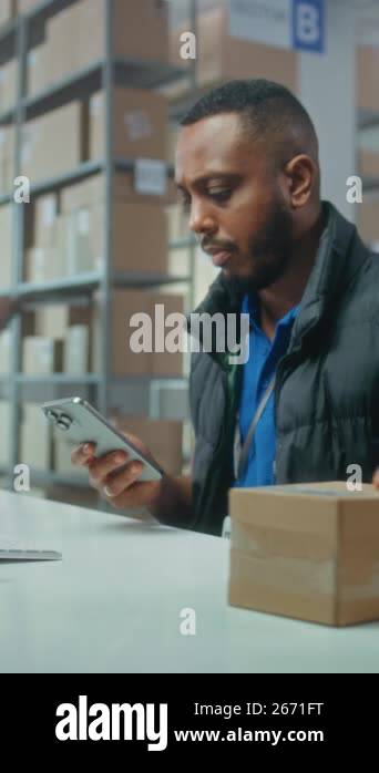 African American logistics manager scans parcels using smartphone, works in postal service ...