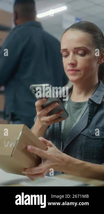 Female logistics specialist scans parcels using smartphone, prepares packages for shipping ...