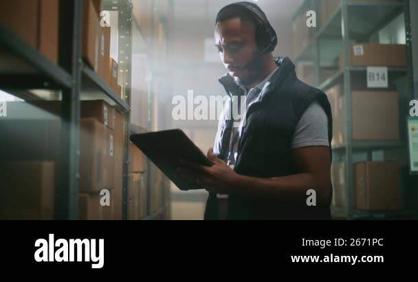 African American Inventory Manager in Headset Uses Tablet Computer to ...