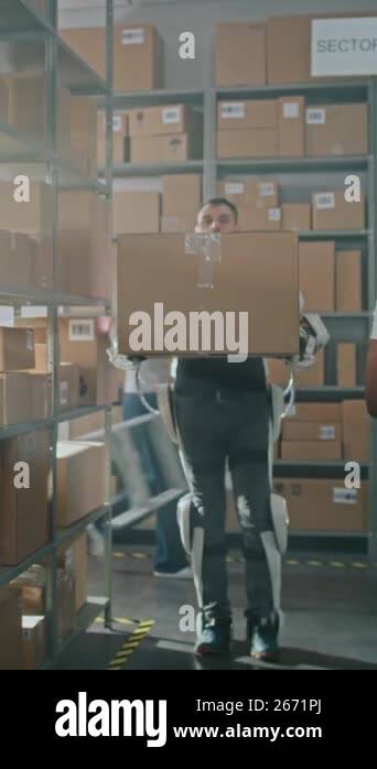 Advanced Warehouse: Sorting Center Worker in Futuristic Full Body Powered Exoskeleton Places ...