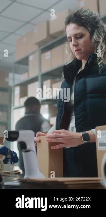 Female Warehouse Clerk Packs Cardboard Box with Online Order, Scans Code, Uses Tablet Computer ...