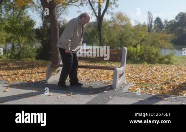 An older man with glasses and a beard sits in a park during autumn ...