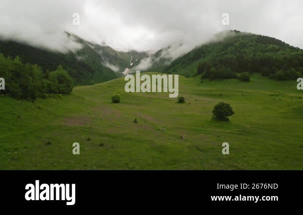 Aerial view solo backpacker hiking in alpine meadow. Green hills, misty ...
