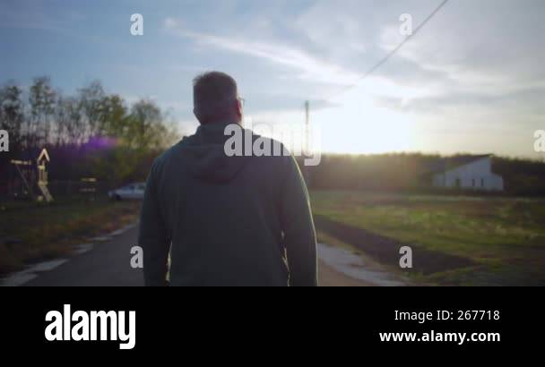 Man walking on a quiet rural road, looking back over his shoulder ...