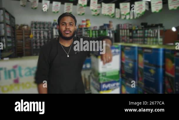 Confident store clerk leaning on stacked paint cans in a hardware store ...
