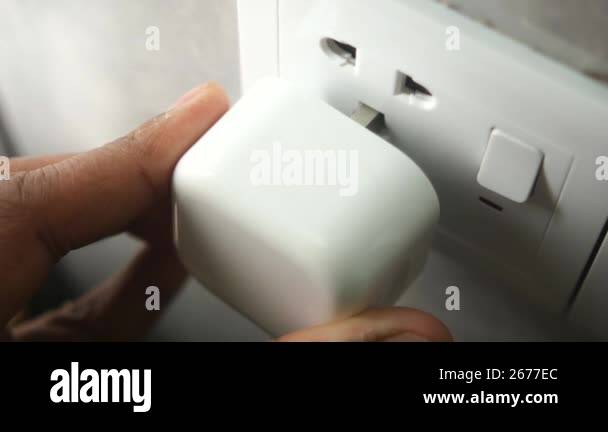 A hand inserts a charger into a wall outlet, showing the electrical ...