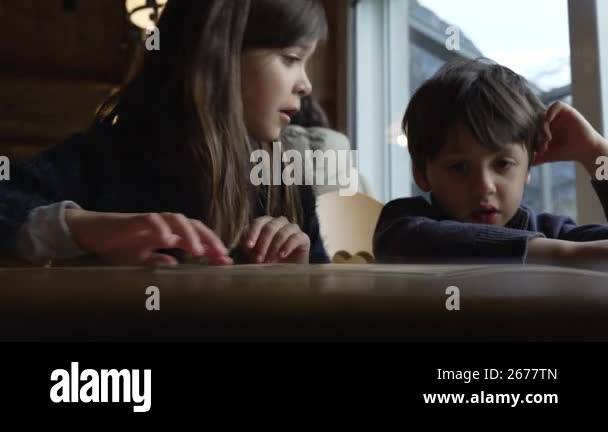 Young siblings looking at restaurant menu, sister assisting younger ...