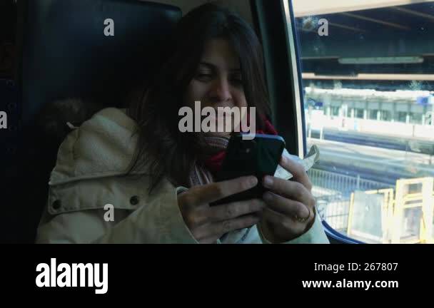 Female passenger using cellphone device by train window. Woman wearing ...
