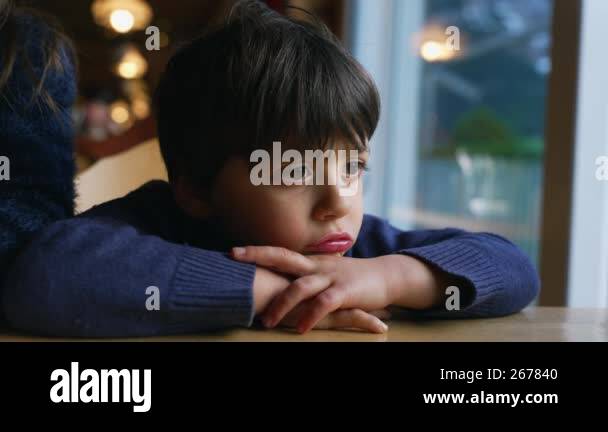 Pensive child feeling boredom at restaurant, leaning on table ...