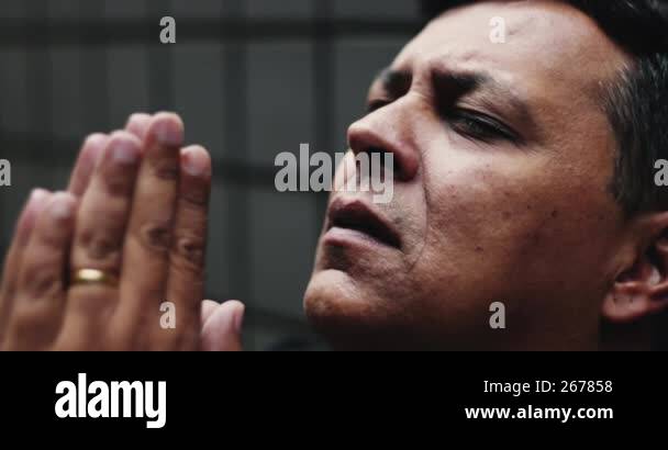 Man praying with hands joined, eyes closed, facial expression conveying ...