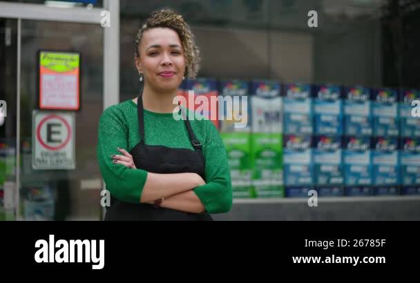 Female shopkeeper with curly hair wearing an apron standing in front of ...