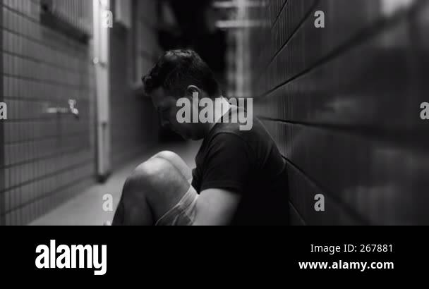 Man sitting alone in narrow alley, head bowed in deep reflection ...