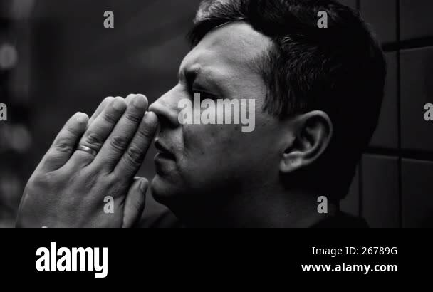 Man praying in emotional crisis, hands clasped near face, seeking ...