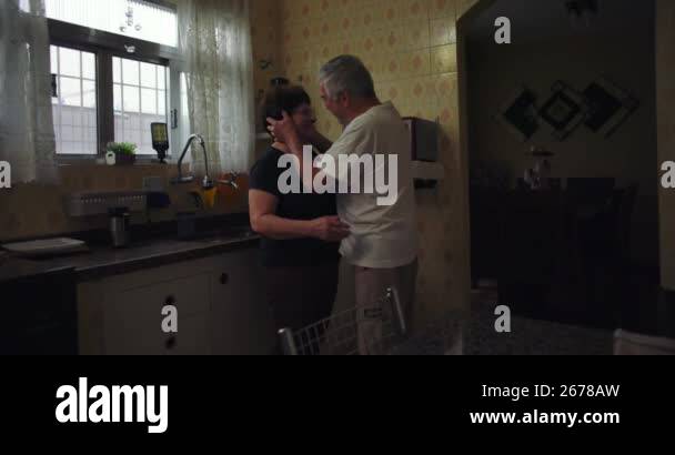 Elderly couple hugging warmly in kitchen, heartfelt connection and affection, casual indoor ...