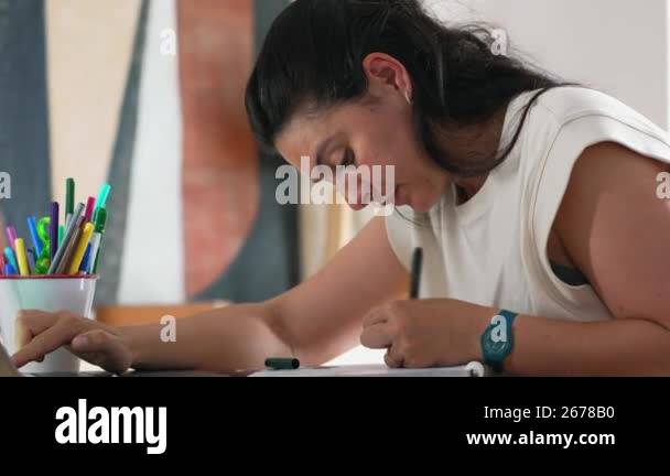 Woman intensely focused on studying and writing at a desk with a laptop ...