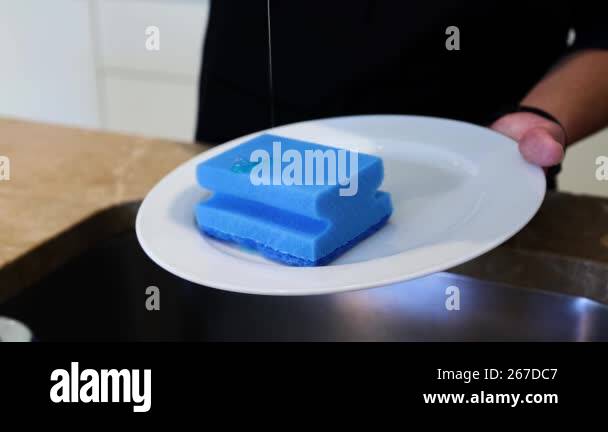 Close up of male hands putting liquid soap on a sponge to wash a dish ...