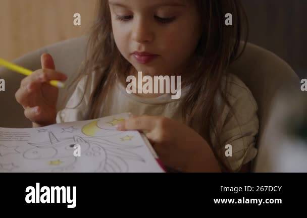A young girl engrossed in coloring designs in her sketchbook with a bright yellow pencil ...