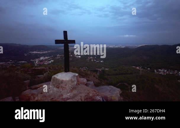 A solitary cross stands on a mountain peak overlooking a vast green ...