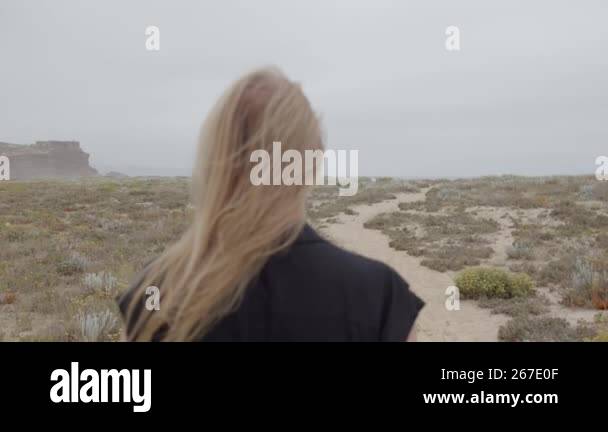 Blonde woman filmed from the back with no face visible walking along ...