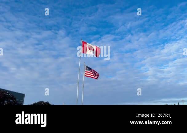 the Canadian flag and the United States flag flutter in the wind on a ...