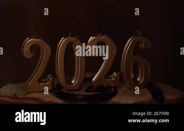 On a dark background, a birthday cake decorated with cream and the numbers of the year 2026 ...