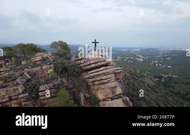 Black cross standing on a rocky cliff overlooking a vast valley with ...