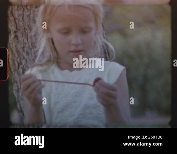 Vintage scene of a little blonde girl playing with a red licorice candy ...