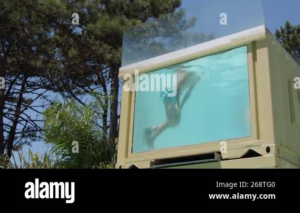 Swimmer executing acrobatic moves within transparent, elevated pool ...