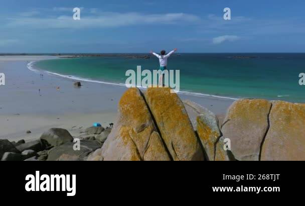 Young guy standing on huge stones on the shore of the Atlantic Ocean on ...