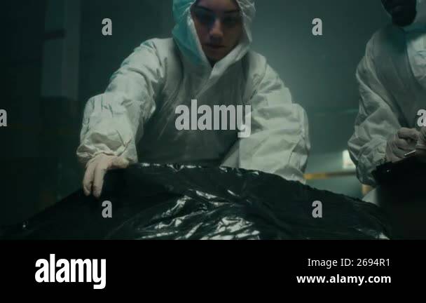 Lowkey shot of young Caucasian female forensic expert unzipping black ...