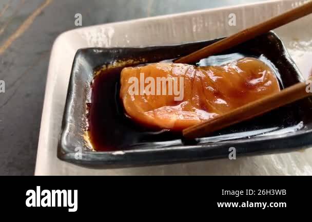 Wood chopsticks holding a salmon cut in soy sauce with a soy splash ...