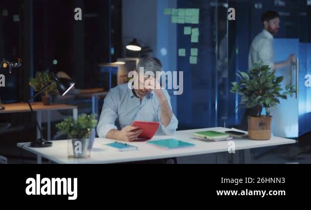 Exhausted business boss sitting on office desk using tablet computer ...